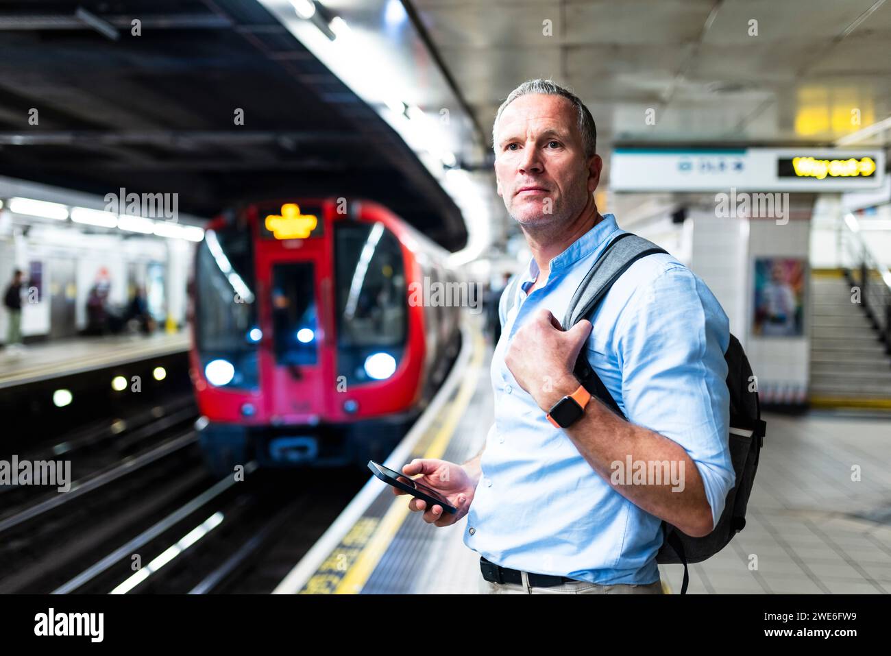 Mature businessman holding smart phone and waiting for train on ...