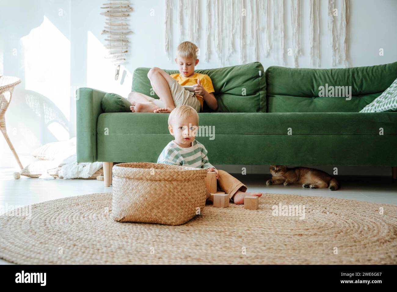 Boy sitting on carpet in living room at home with brother in background ...