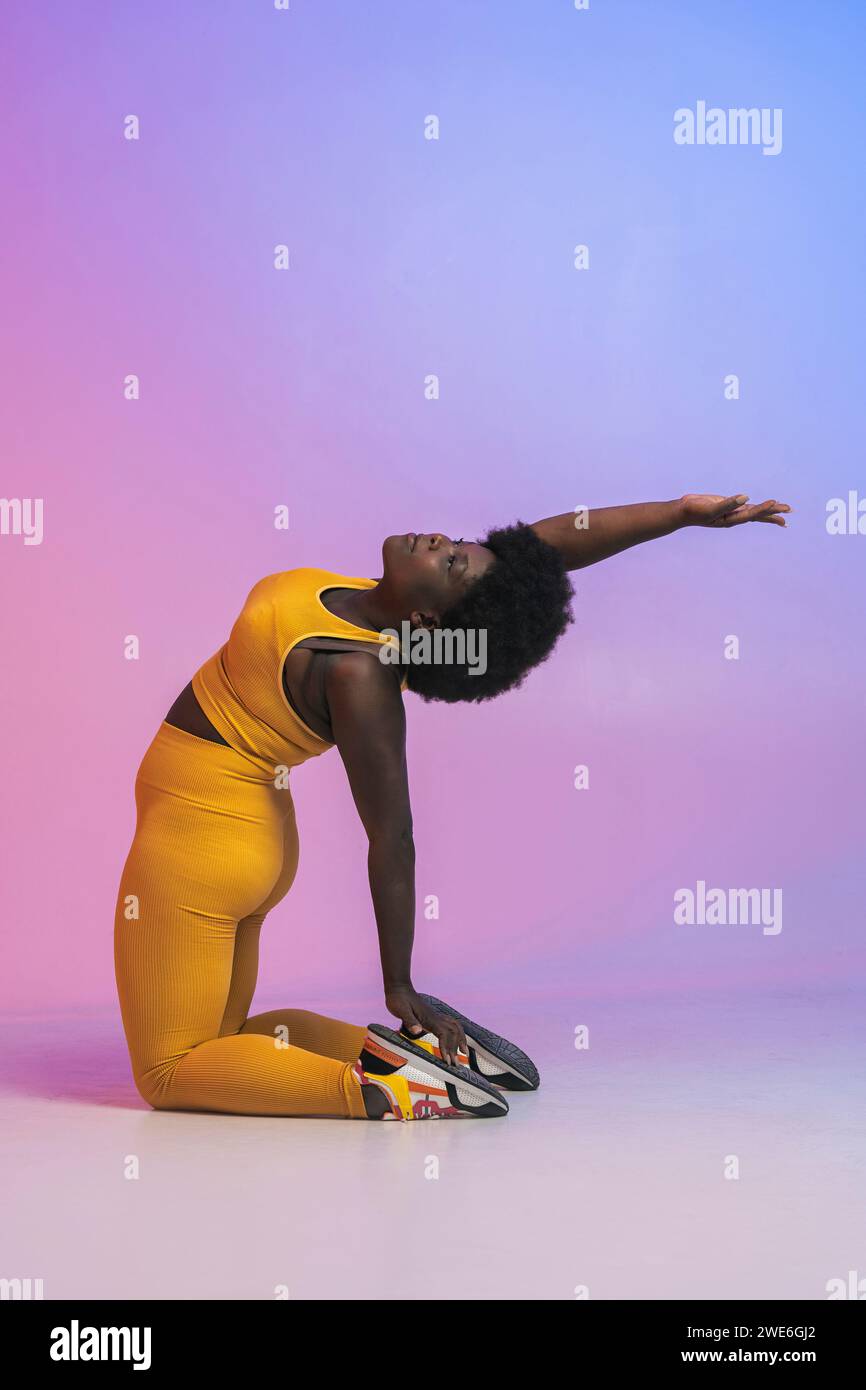 Flexible young woman in yellow sports clothing stretching against two ...