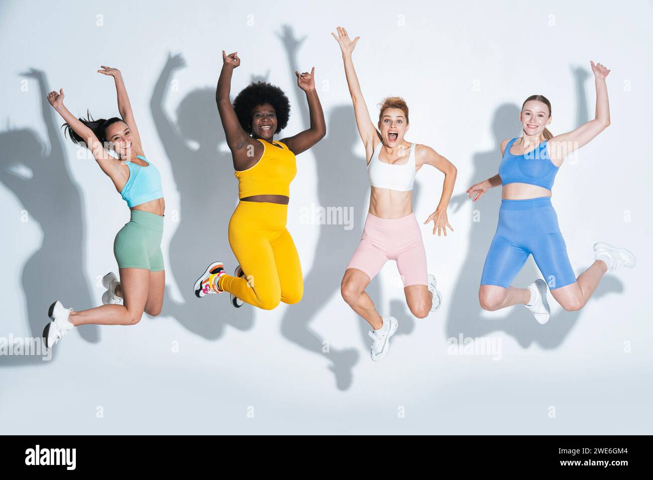 Excited multiracial female friends jumping together against white ...