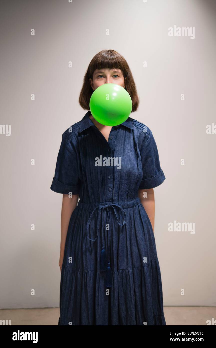Young woman blowing green balloon in front of wall Stock Photo - Alamy