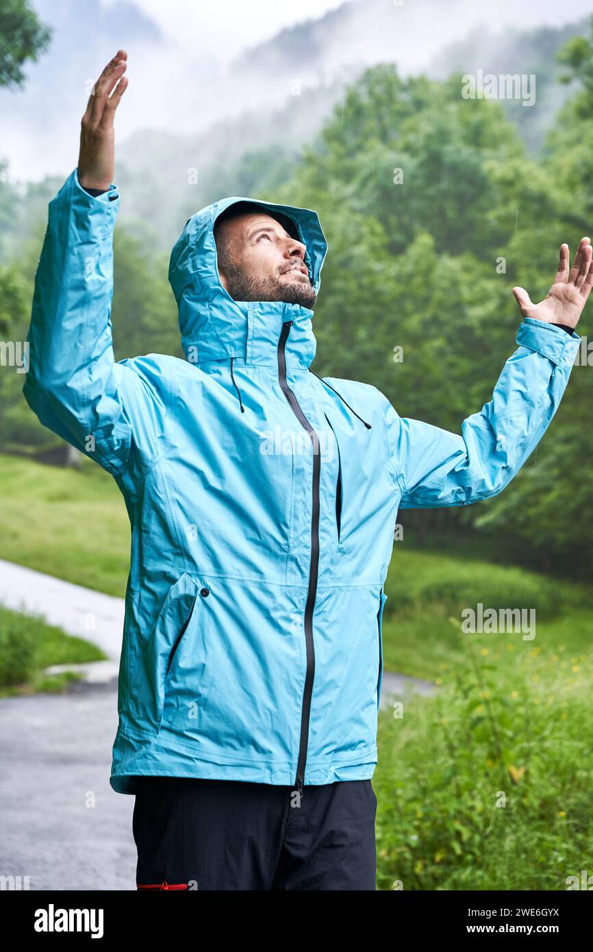 Smiling man wearing blue jacket and standing with arms raised in front ...