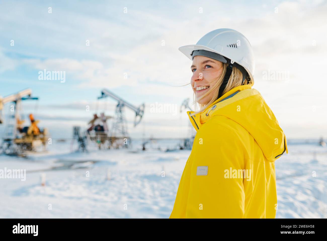 Smiling young engineer wearing hardhat at oil production field in ...