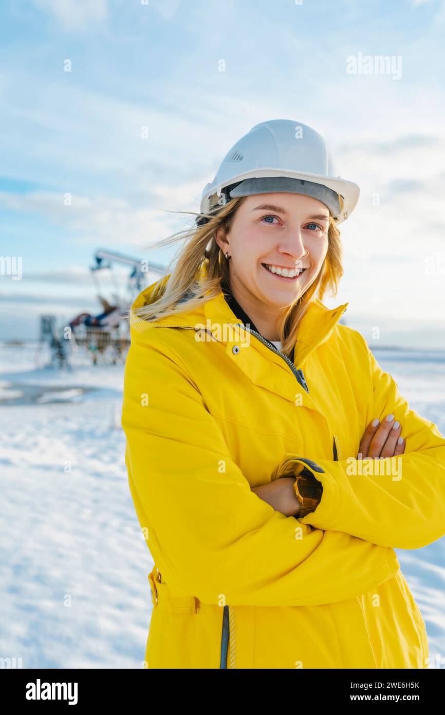 Smiling engineer with arms crossed at oil production field in winter ...