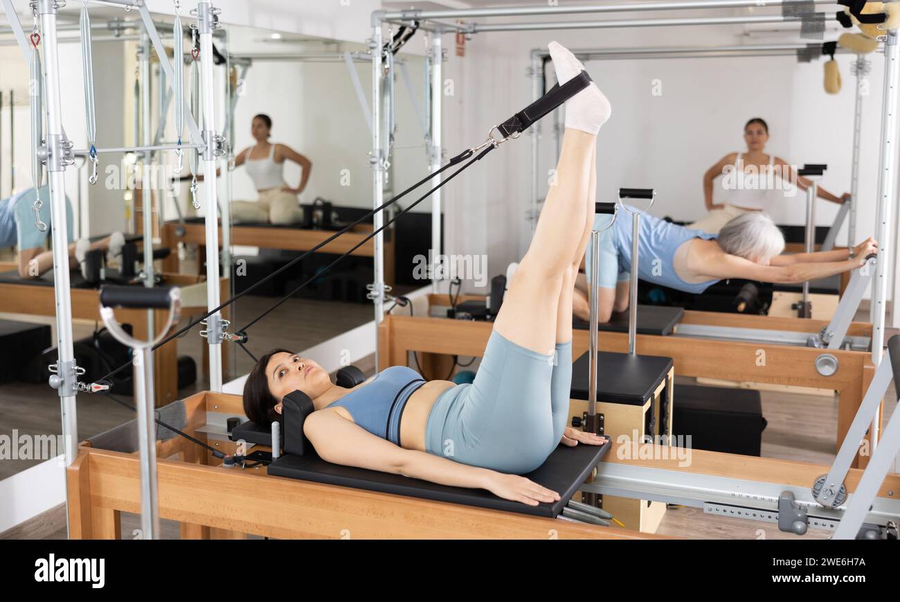 Positive woman practicing pilates stretching exercises on reformer at ...