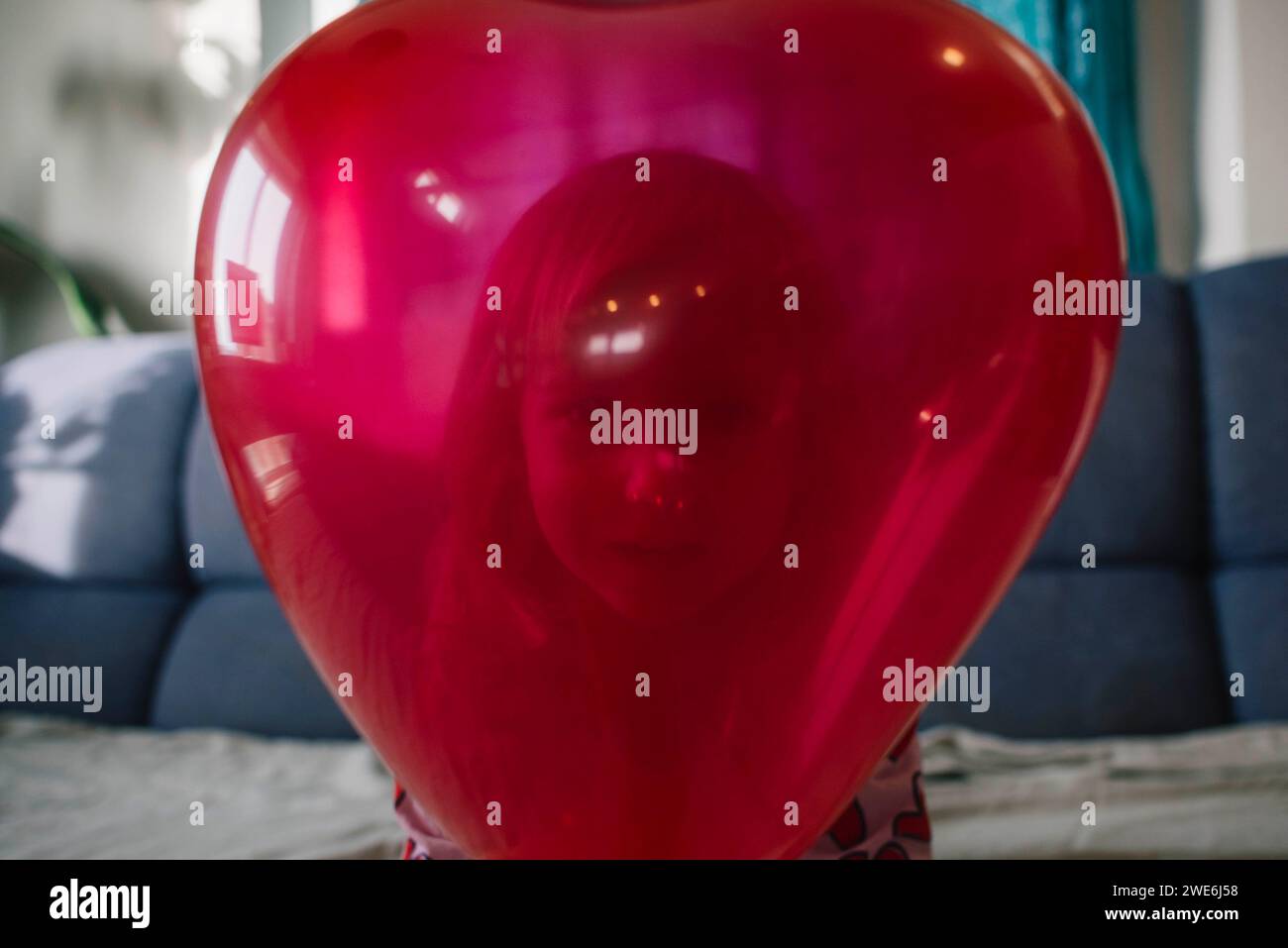 Girl looking through red balloon at home Stock Photo - Alamy