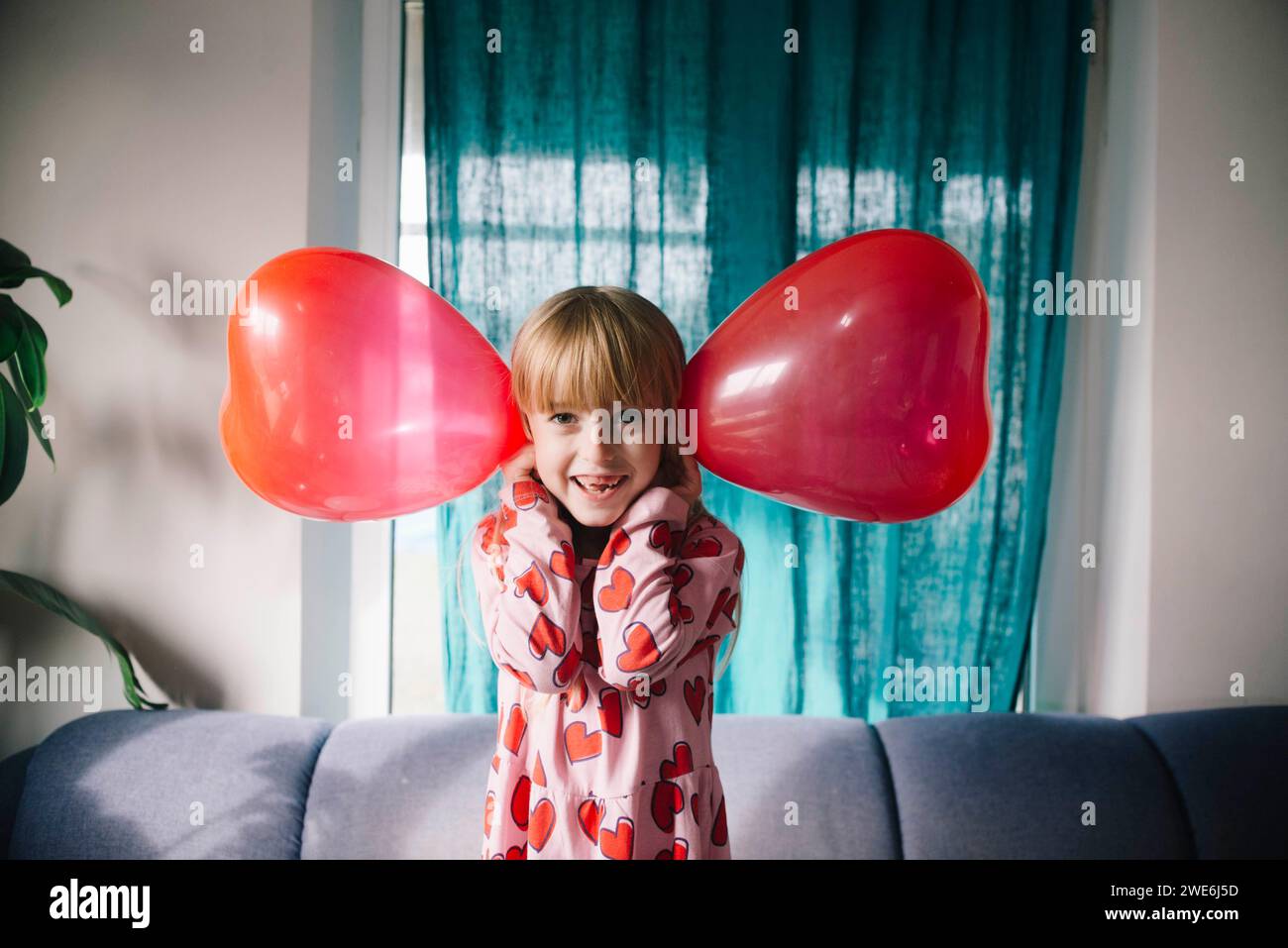 Playful girl holding balloons over ears at home Stock Photo - Alamy