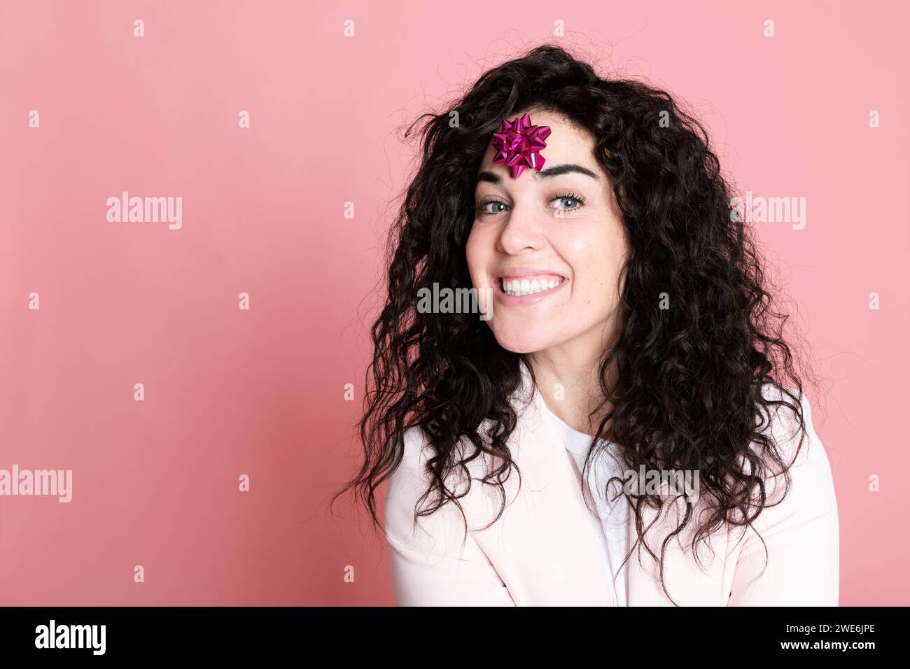 Happy young woman with tied bow on forehead against pink background ...