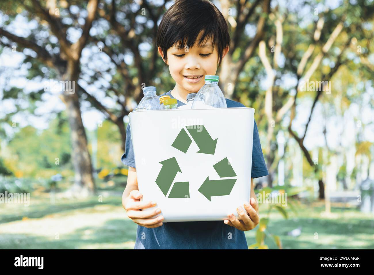 Cheerful young asian boy holding recycle symbol bin on daylight natural ...
