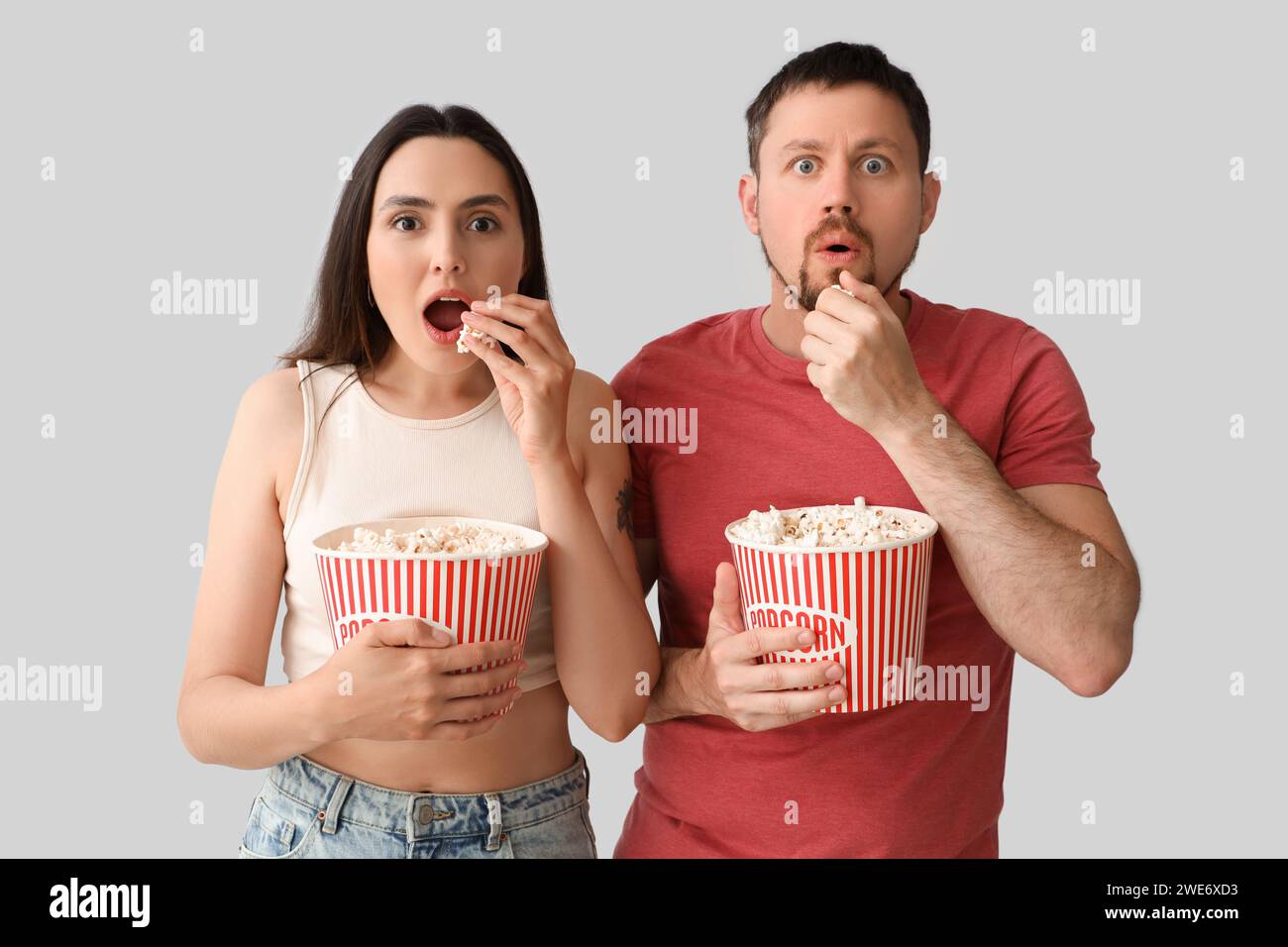 Shocked young couple eating popcorn on light background Stock Photo - Alamy