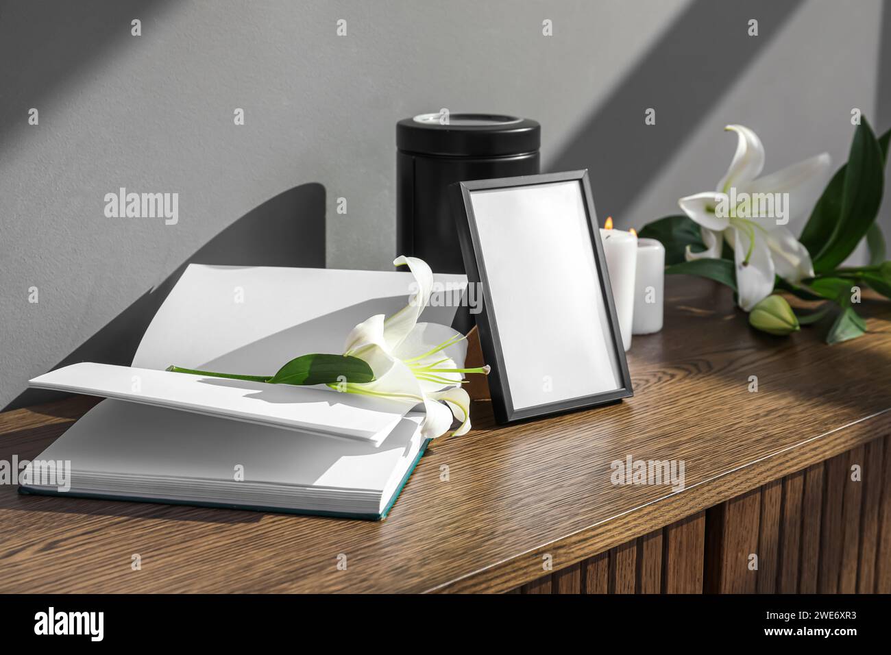 Blank funeral frame, mortuary urn, book and lily flowers on wooden ...