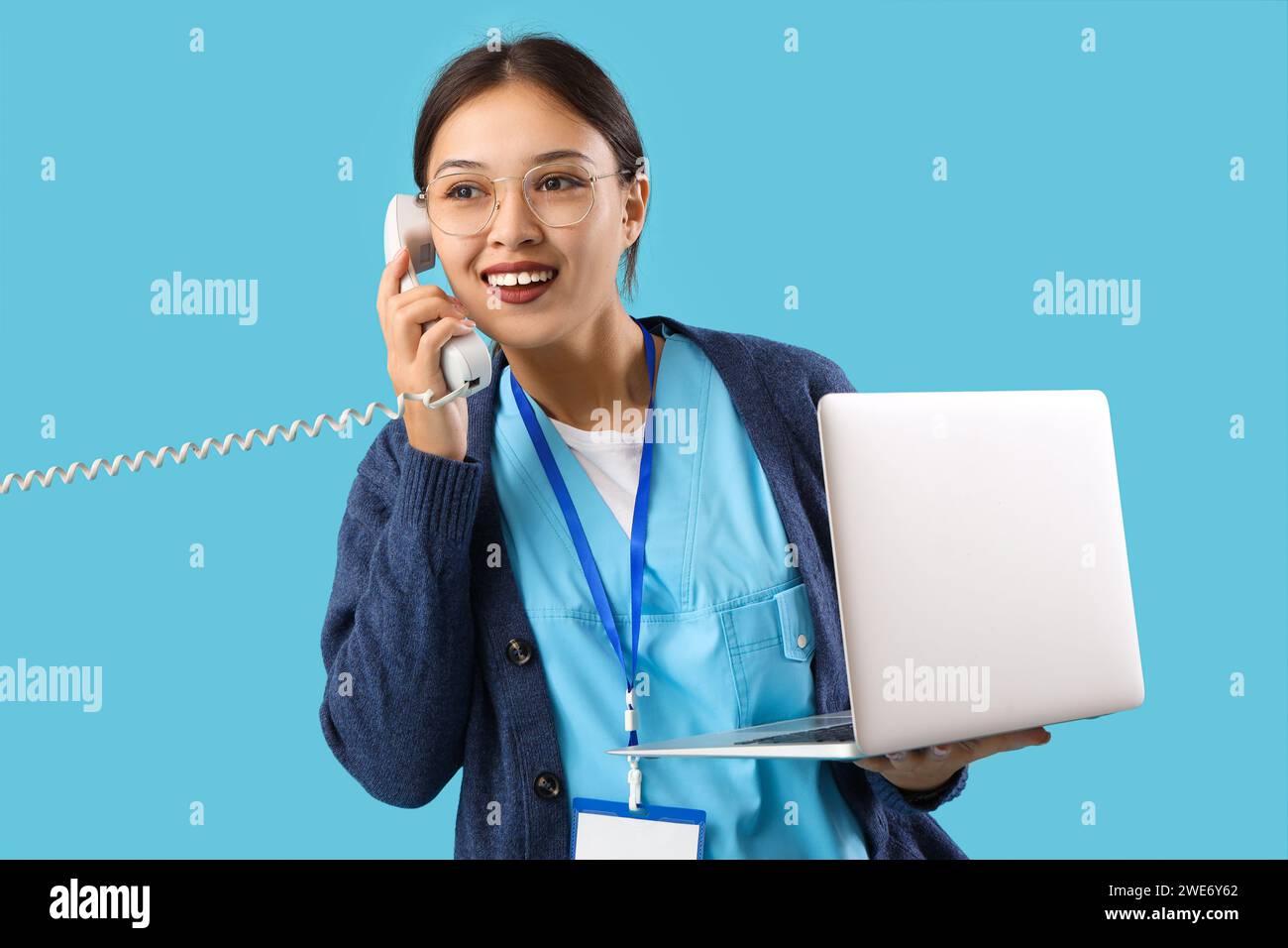 Asian medical intern with laptop talking by telephone on blue ...