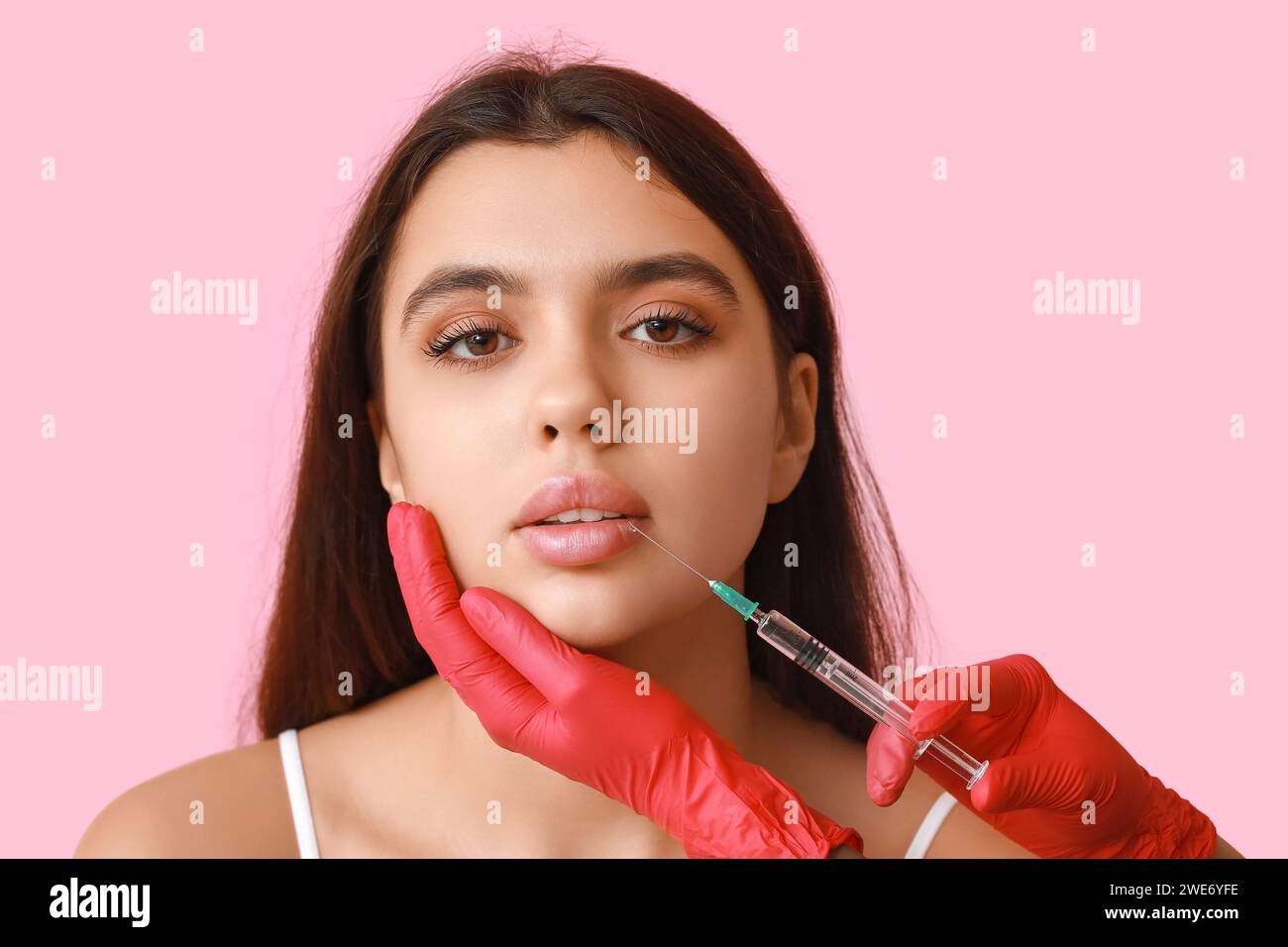 Beautiful young woman receiving lip injection on pink background ...