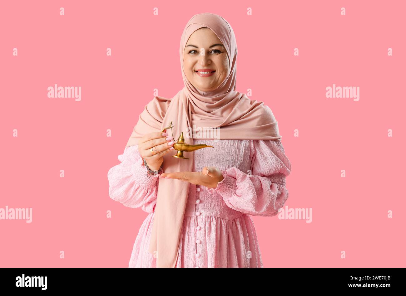Mature Muslim woman with Aladdin lamp on pink background. Ramadan ...