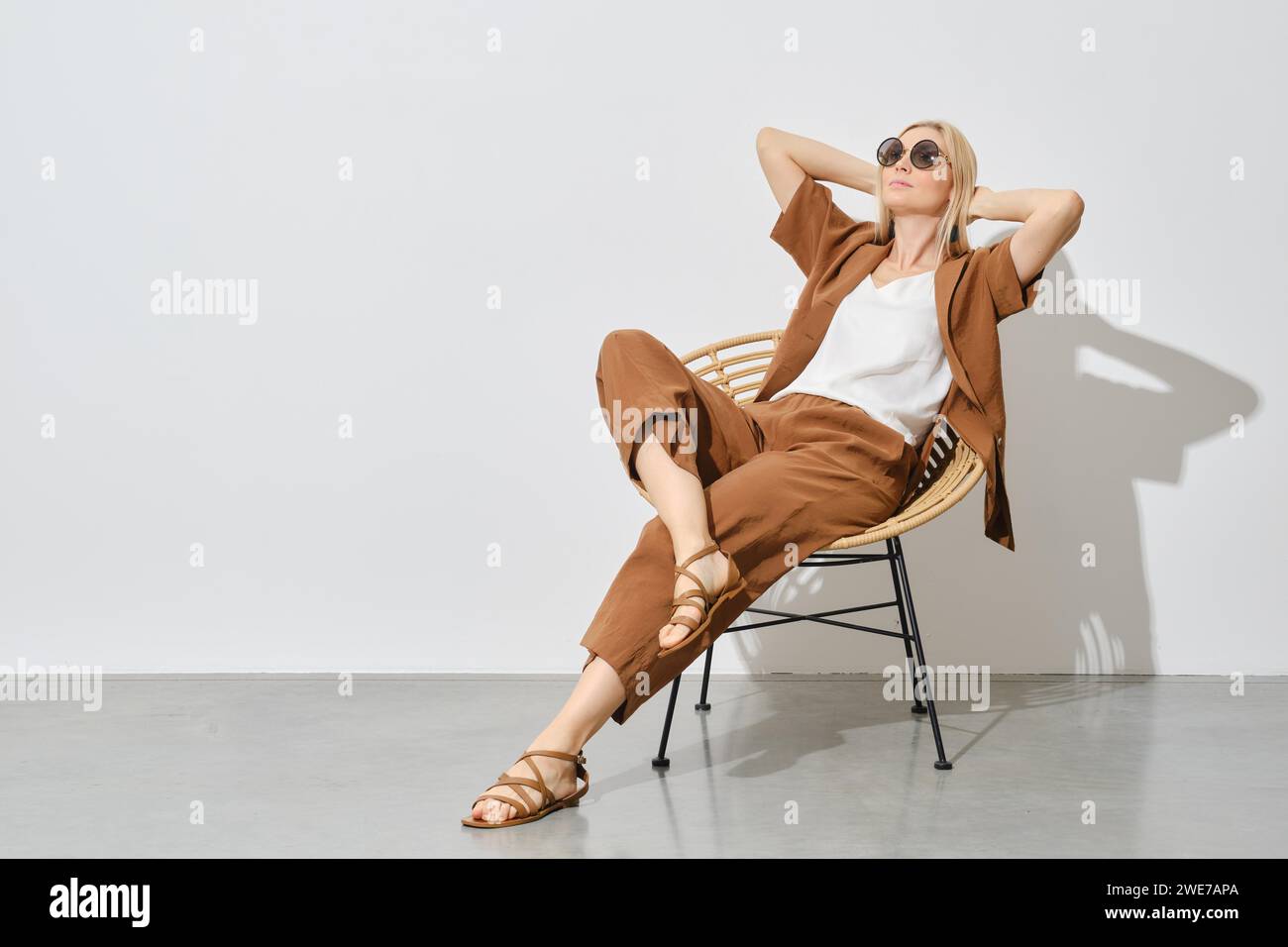 Relaxed blonde woman leans back in a wicker chair with her hands behind ...