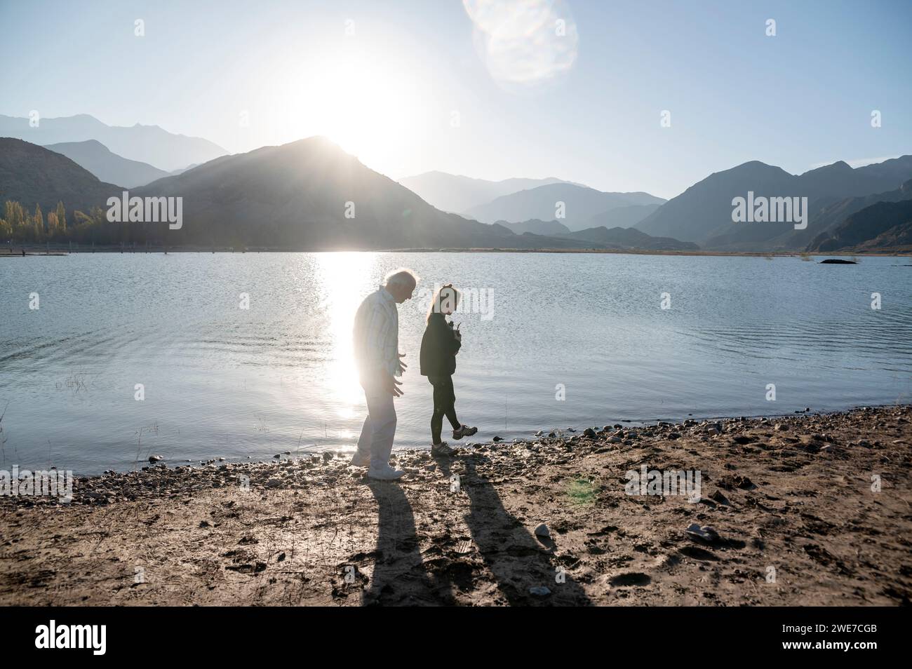 Senior man walking with his granddaughter along the lake shore with ...