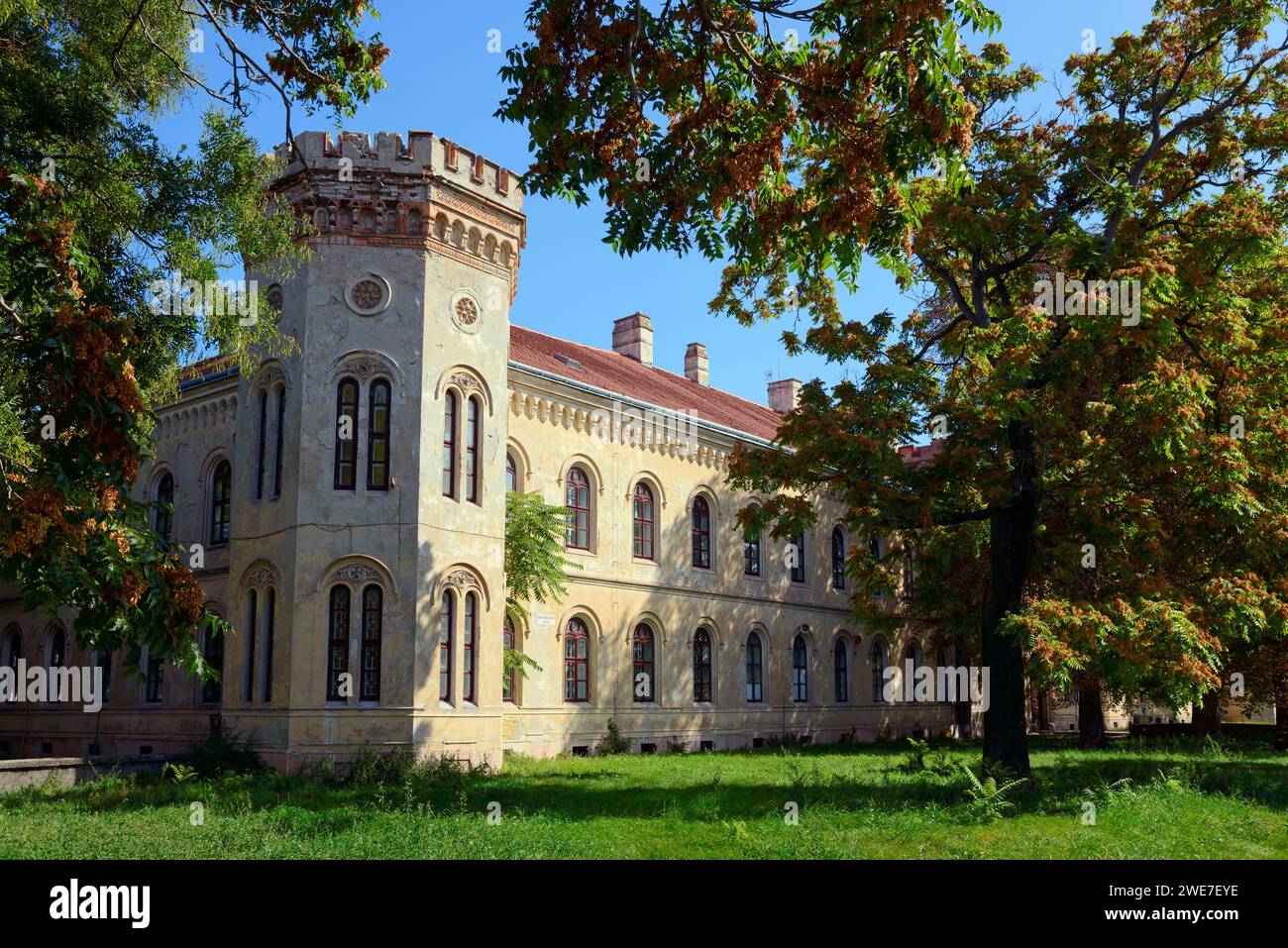 A historic Gothic-style castle surrounded by autumn trees under a clear ...