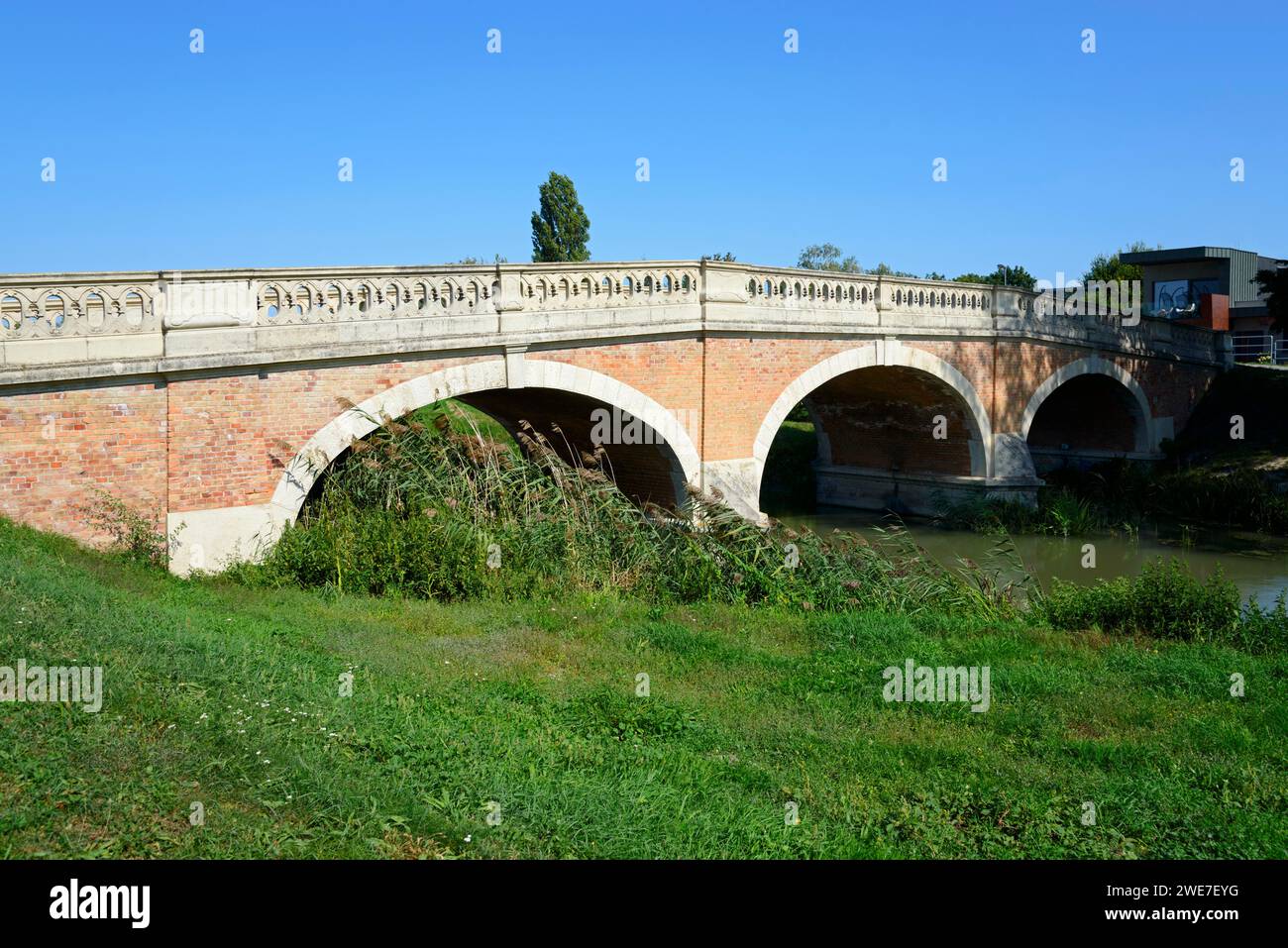A brick arch bridge over a small river in the countryside under a clear ...