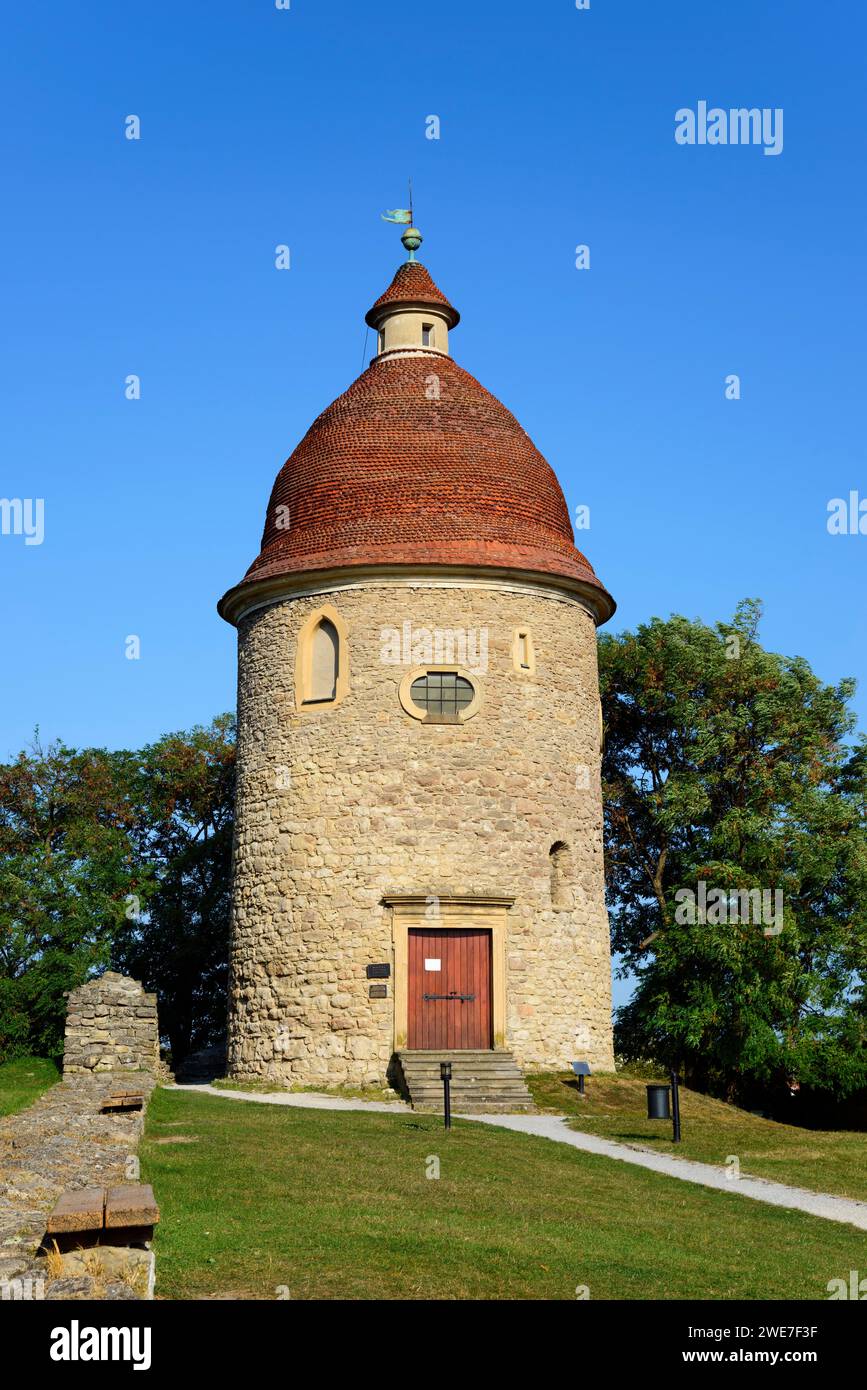 A historic stone tower with a reddish tiled roof under a clear blue sky ...