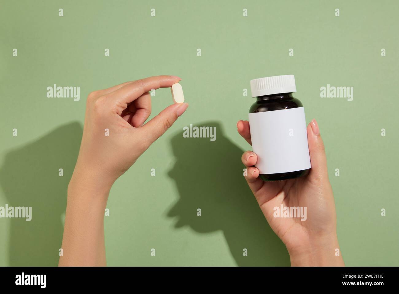 Two hand carrying a small white pill and a blank label medicine bottle ...
