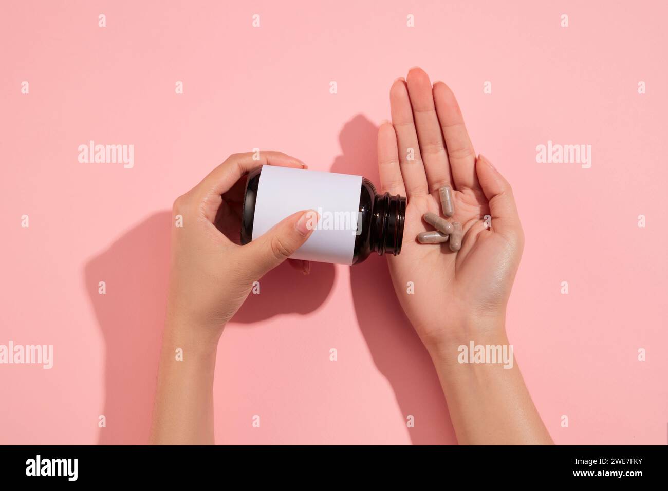 Against a pink background, some capsules are poured into a hand from a ...