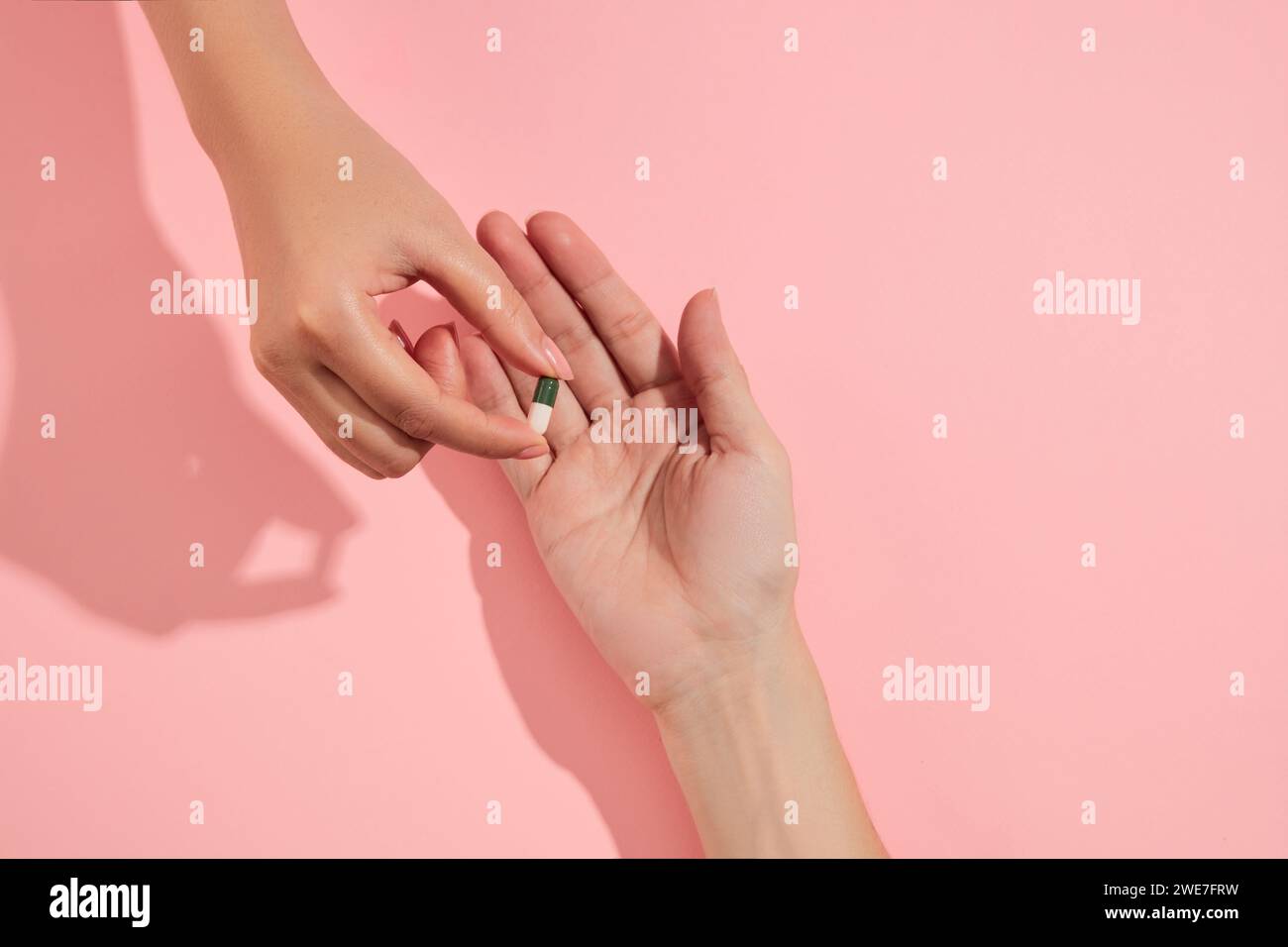 A woman hand giving a green-white capsule to a man hand over the pink ...