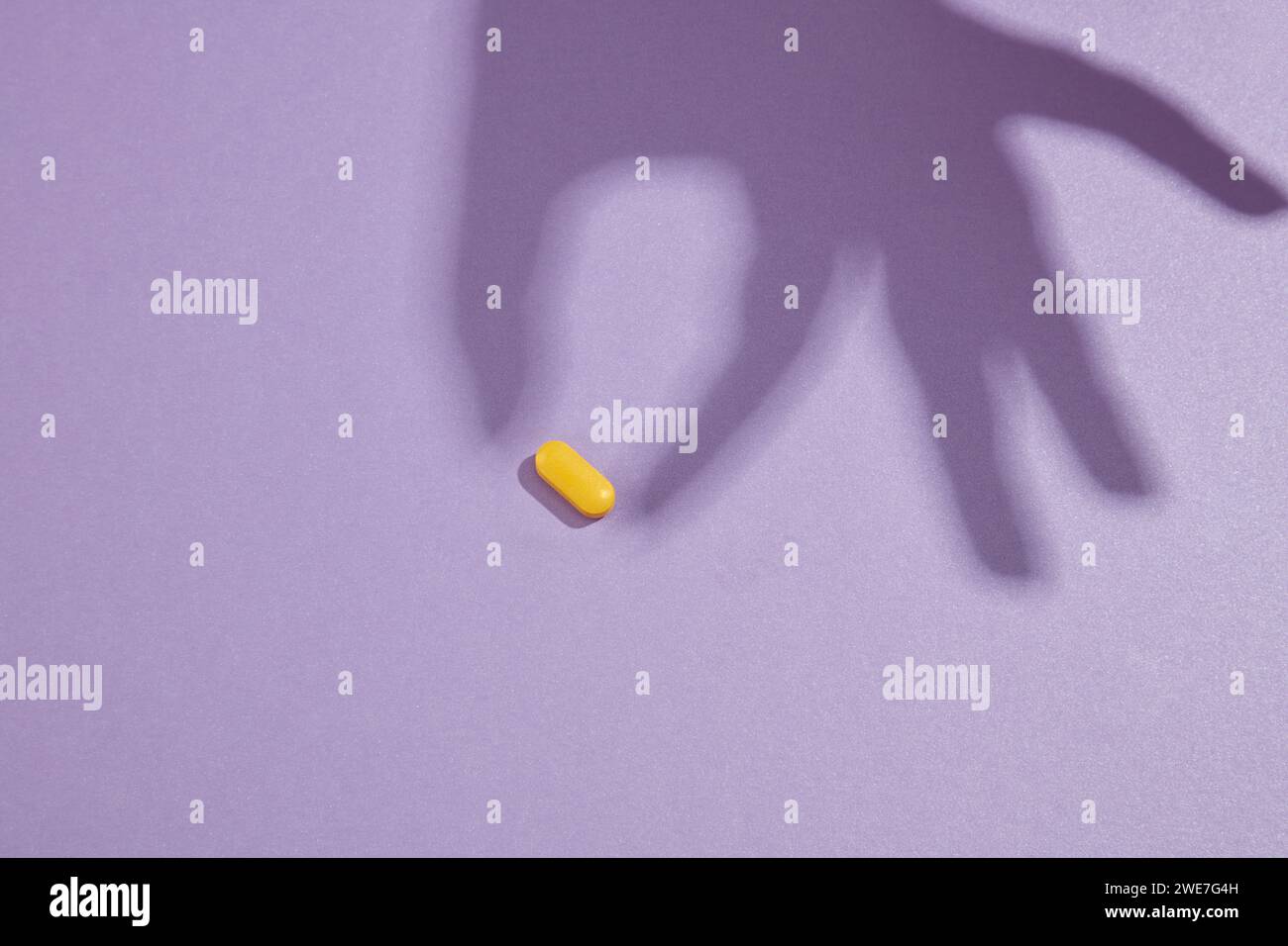 A pill isolated on the purple background with a hand shadow acting like ...
