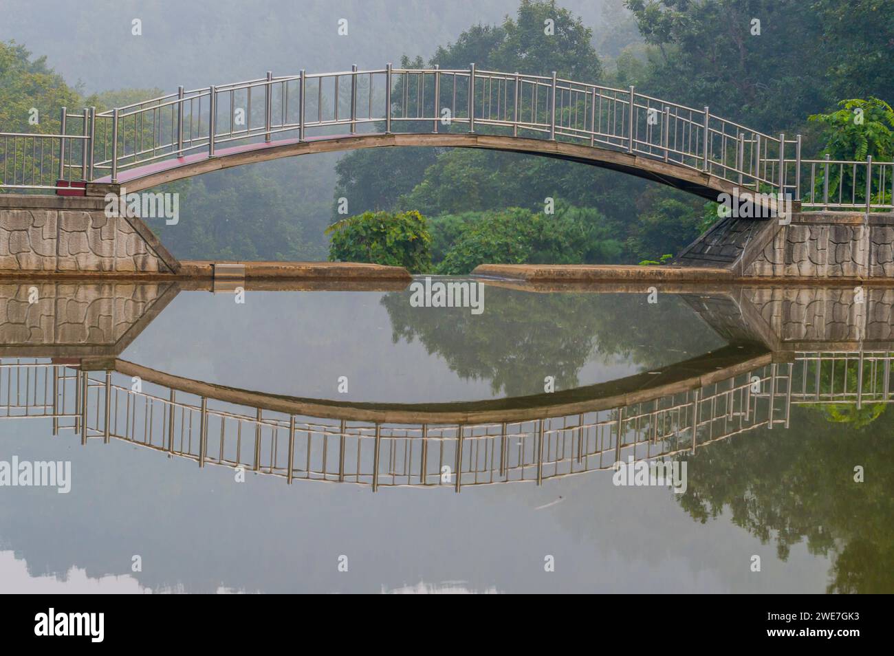 Foot bridge over a small pond with reflection in the water with trees ...