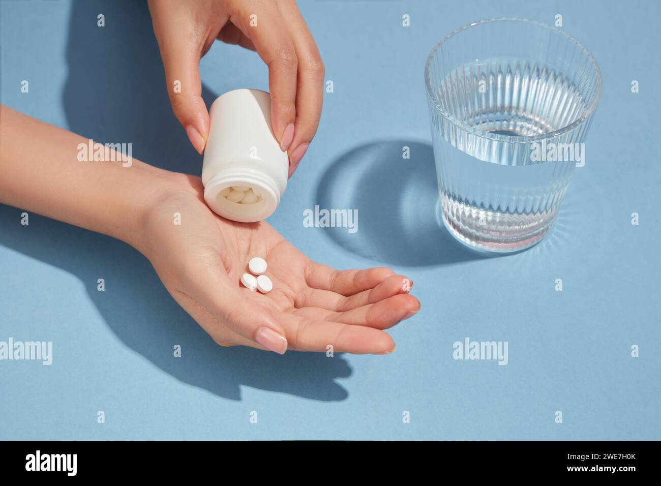 Woman hand model is pouring round tablets into palm. A glass of water ...