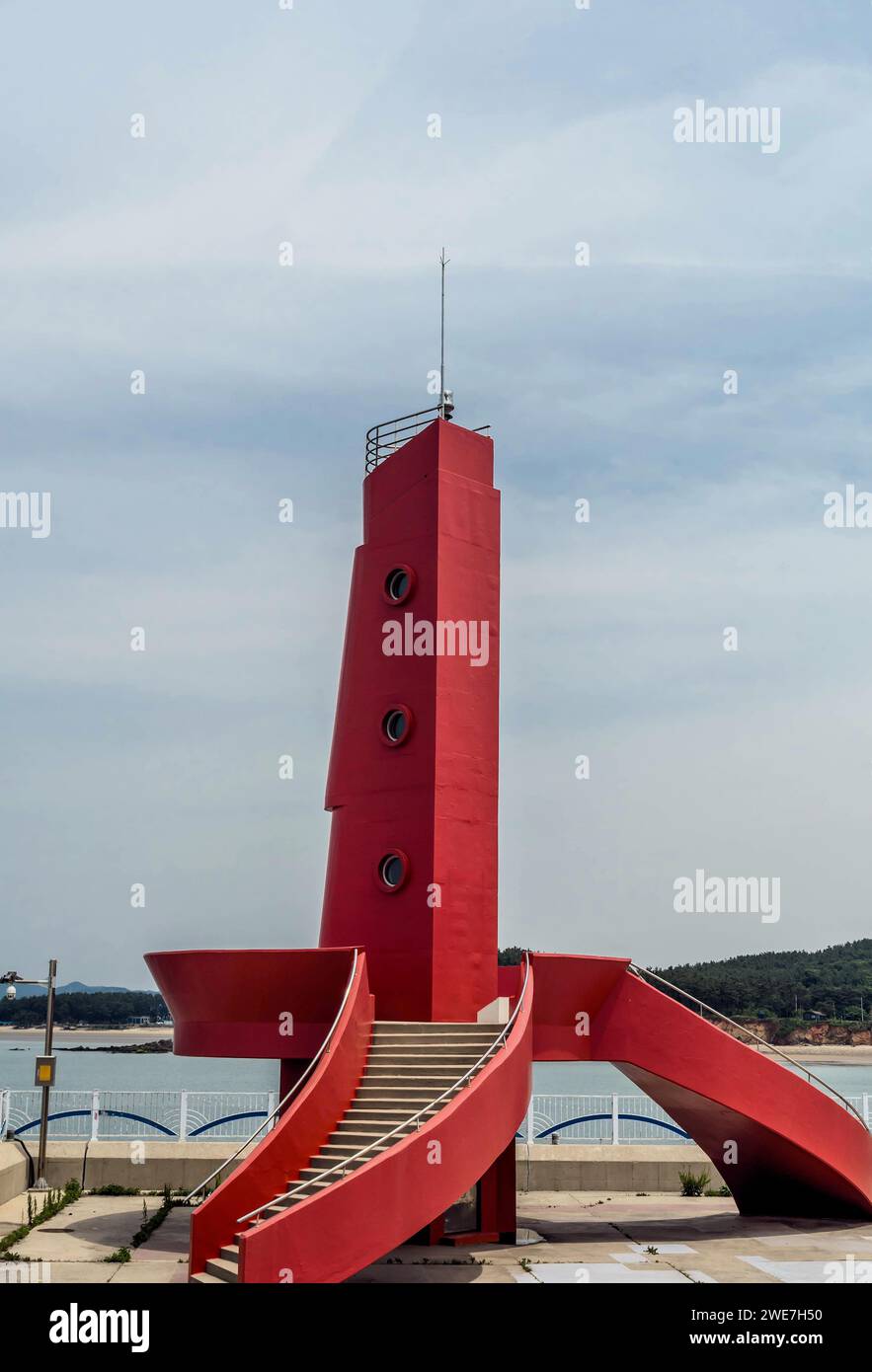 Red lighthouse with curved staircase on concrete dock of seaport in ...