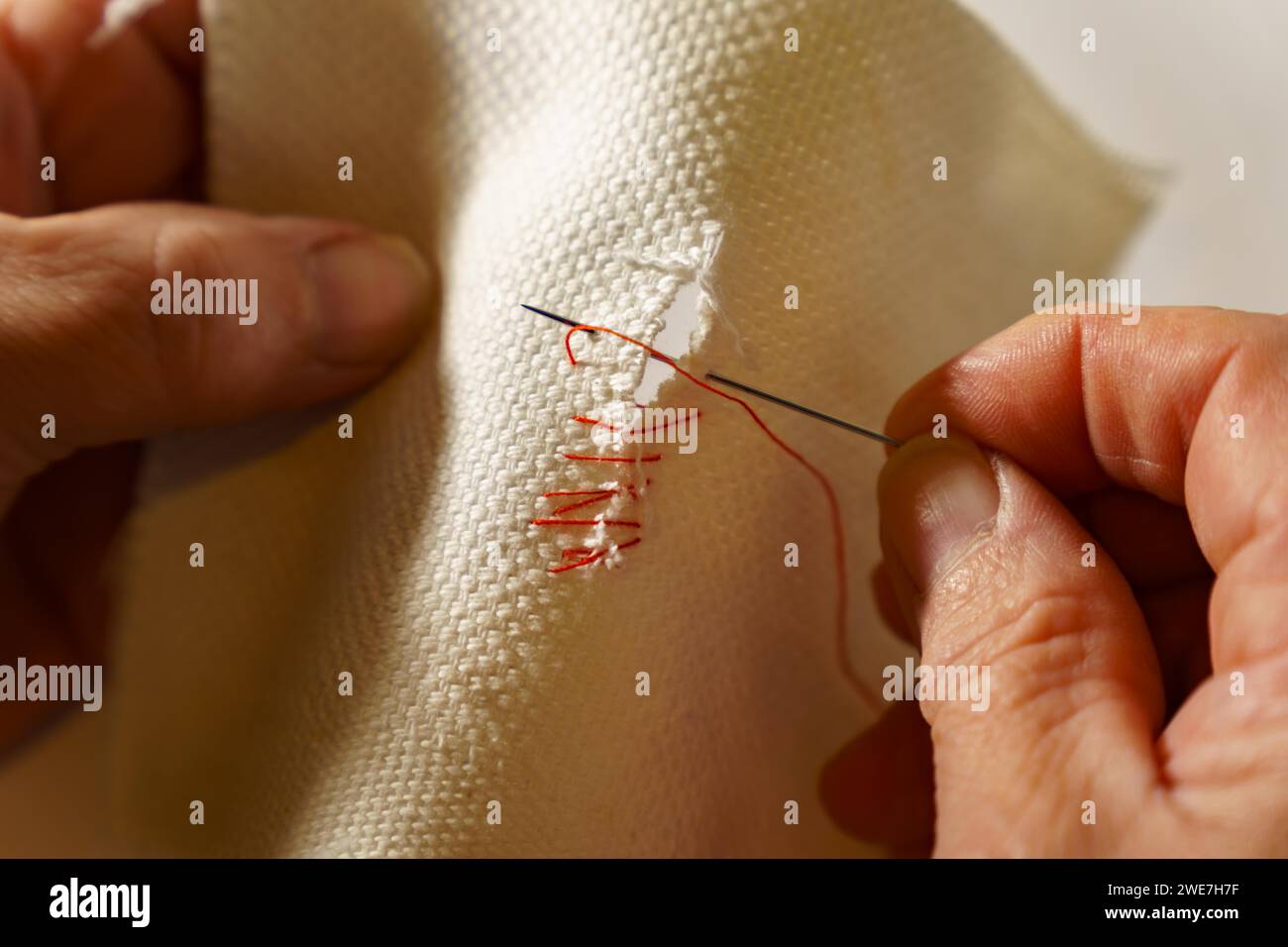 Woman sewing a torn white cloth with red thread Stock Photo - Alamy