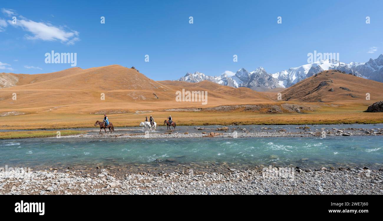 Riders on horses on the river bank, mountain landscape with yellow ...