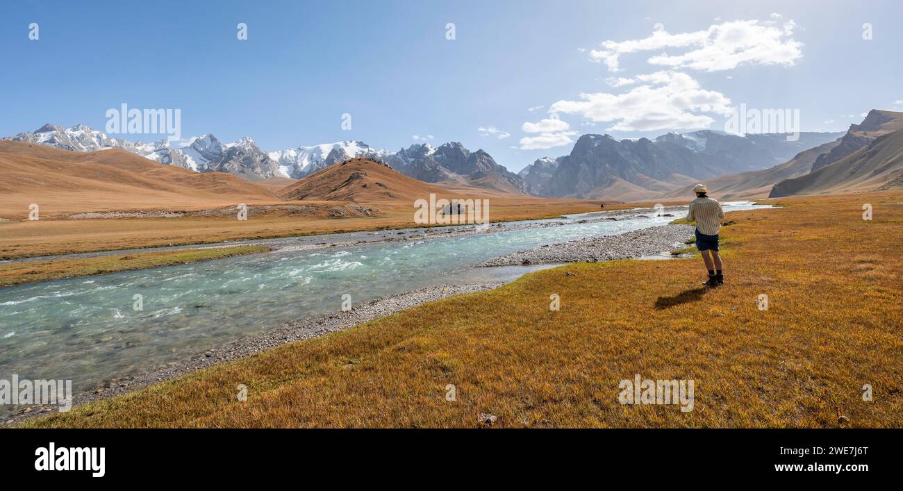 Mountaineer hiking to the mountain lake Kol Suu, mountain landscape with yellow meadows, river ...