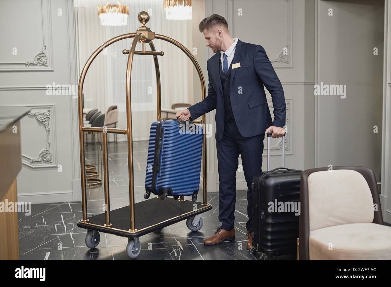Full length portrait of male porter wearing suit helping guests with ...