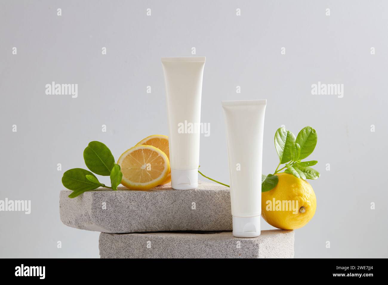Empty label white tubes arranged with fresh leaves and lemon on stone ...