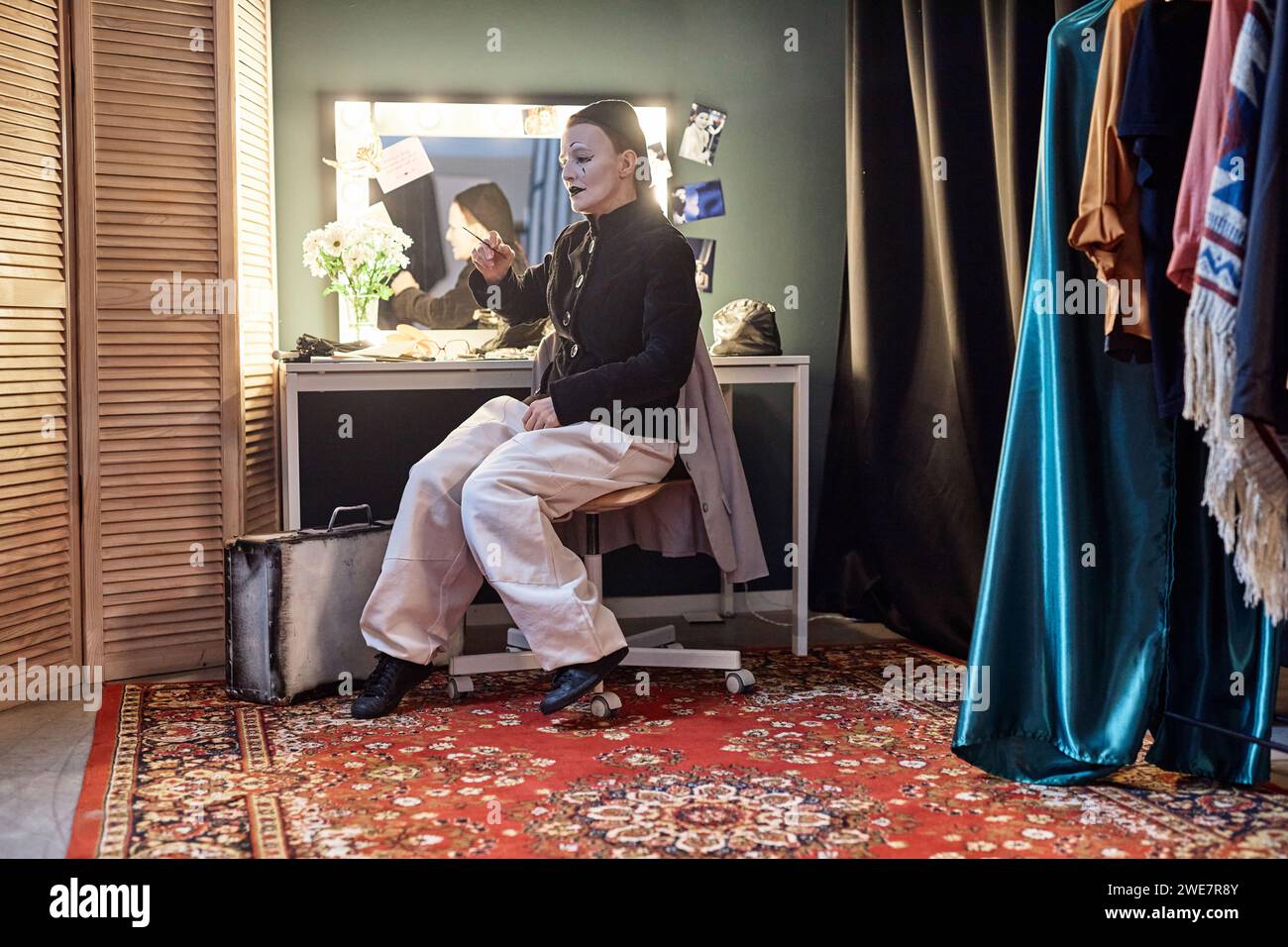 Full length portrait of female mime performer sitting by mirror ...