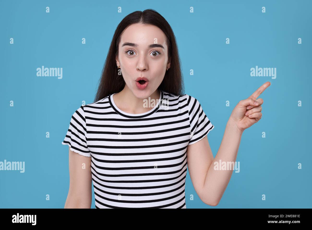 Portrait of surprised woman pointing at something on light blue ...