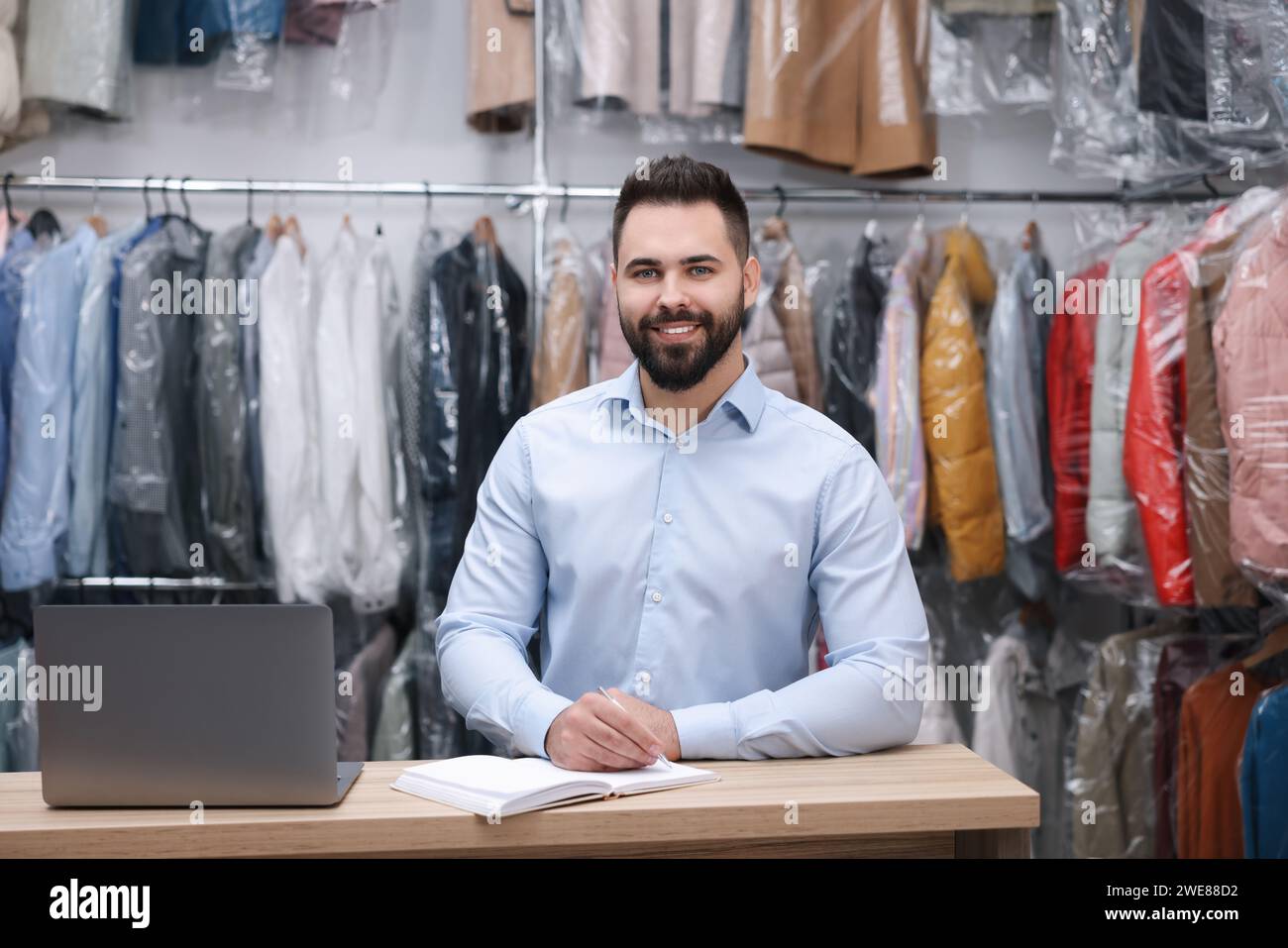 Dry-cleaning service. Happy worker taking notes at counter indoors ...