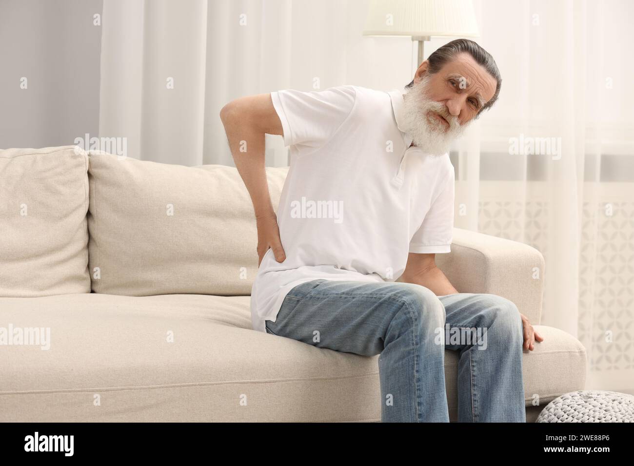 Senior man suffering from back pain on sofa indoors. Rheumatism symptom ...