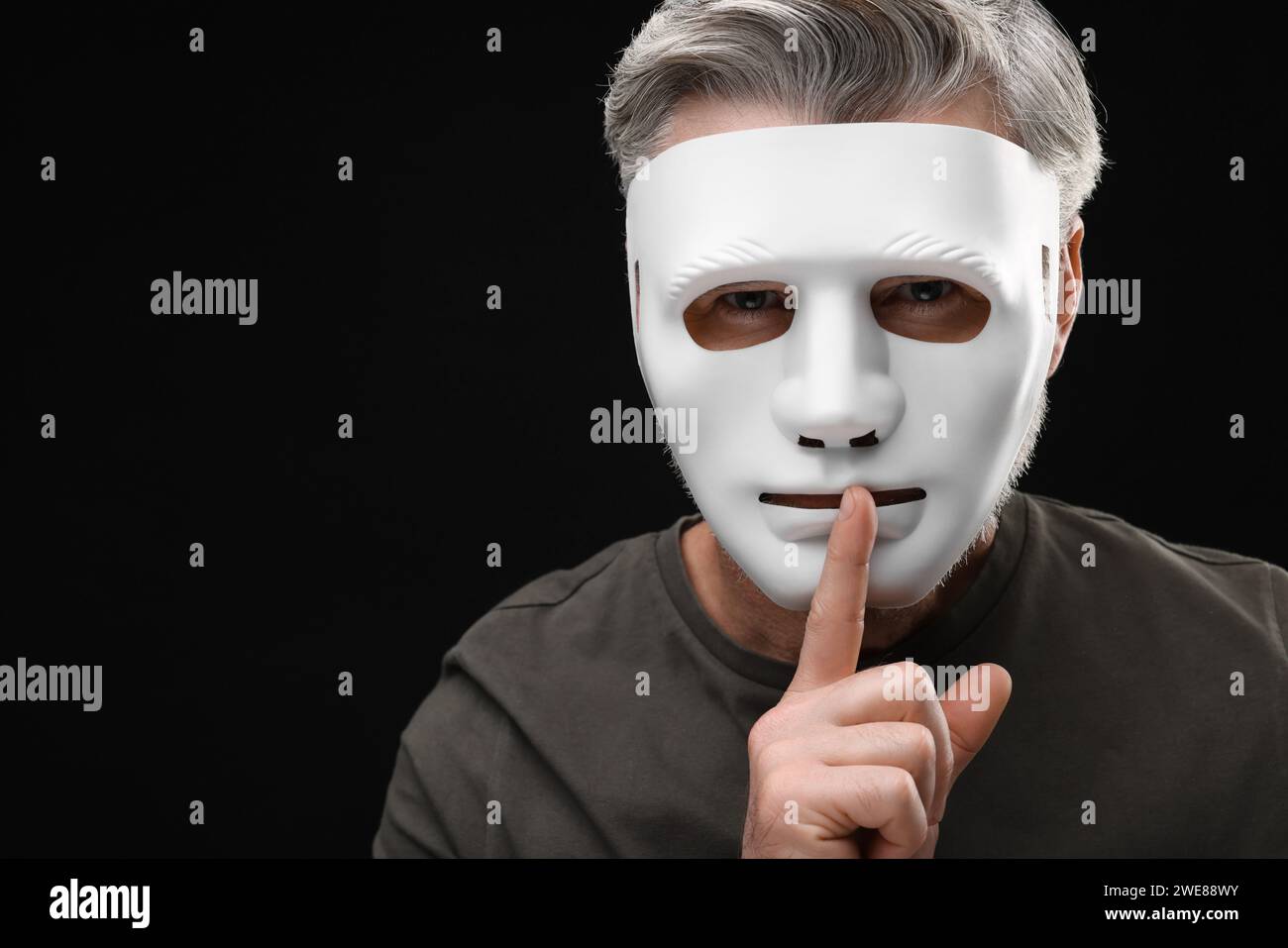 Man in mask showing hush gesture against black background. Space for ...