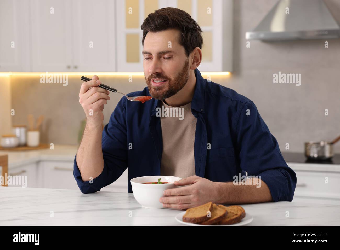 Man eating delicious tomato soup at light marble table in kitchen Stock ...