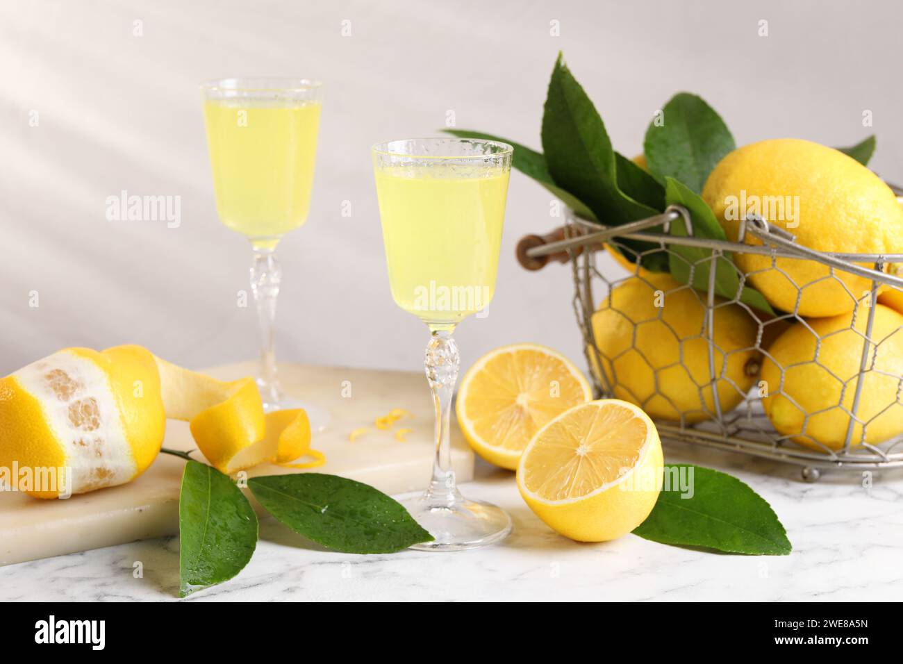 Tasty limoncello liqueur, lemons and green leaves on white marble table ...