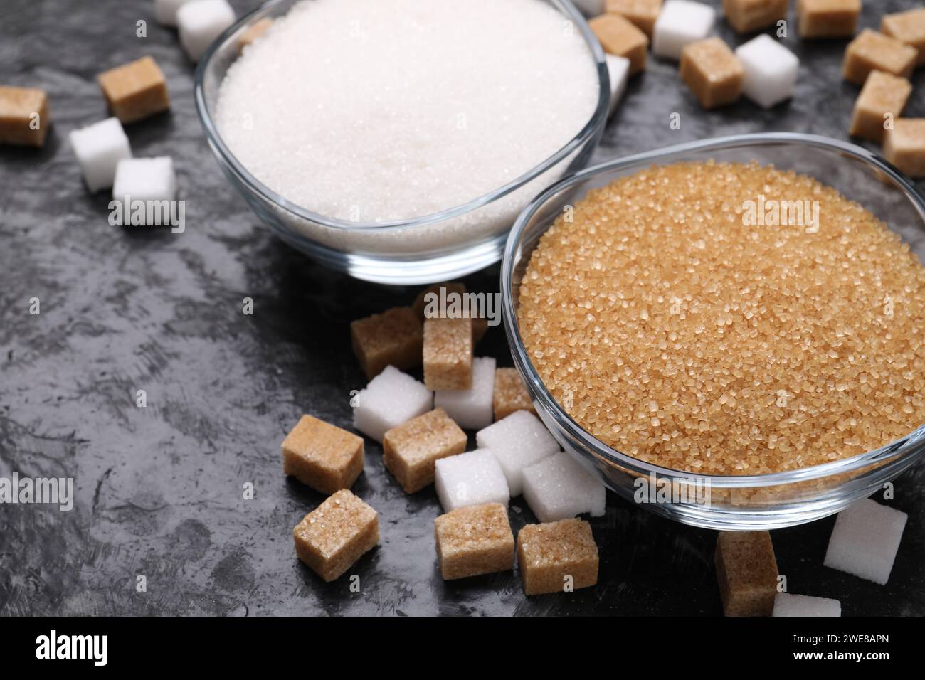 Different types of sugar in bowls on dark gray textured table, closeup ...