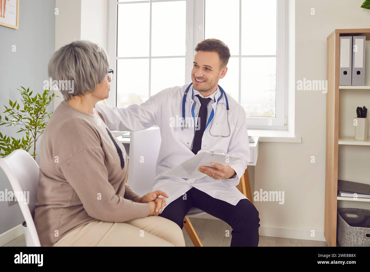 Young smiling doctor clinic visit, male nurse taking care of old woman ...