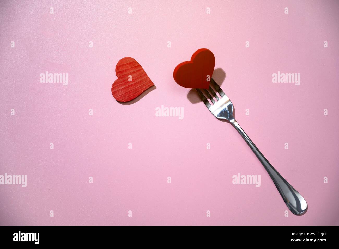 Silverware of fork with a red heart over pink background. Romantic ...