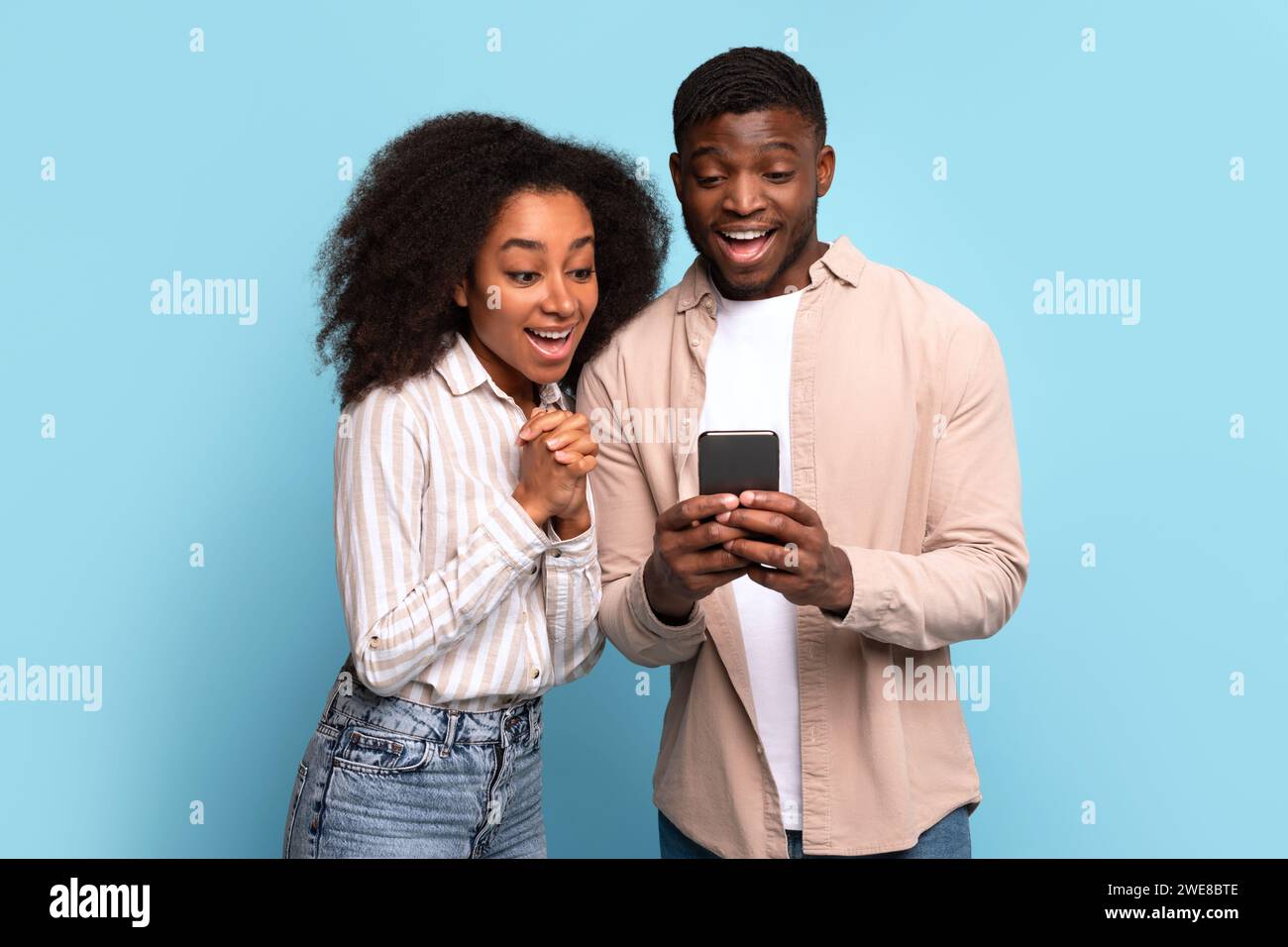 Excited black couple viewing smartphone together on blue background ...