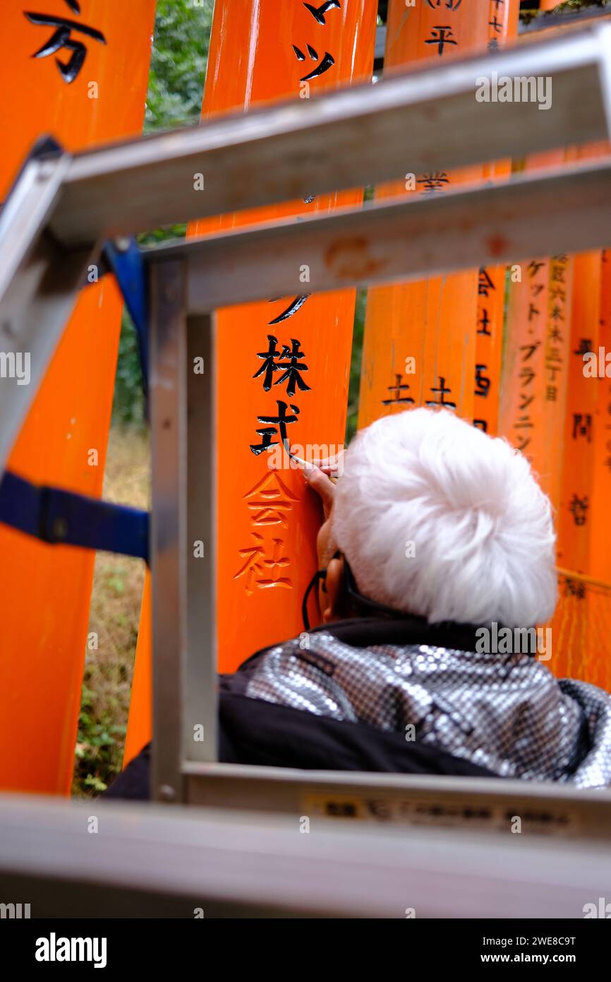 An elder carefully painting the vibrant orange torii gates at Fushimi ...