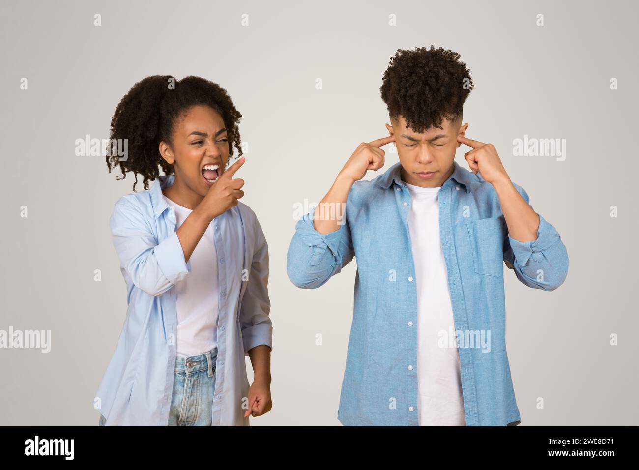 A joyful young woman playfully teases a young man who is plugging his ...