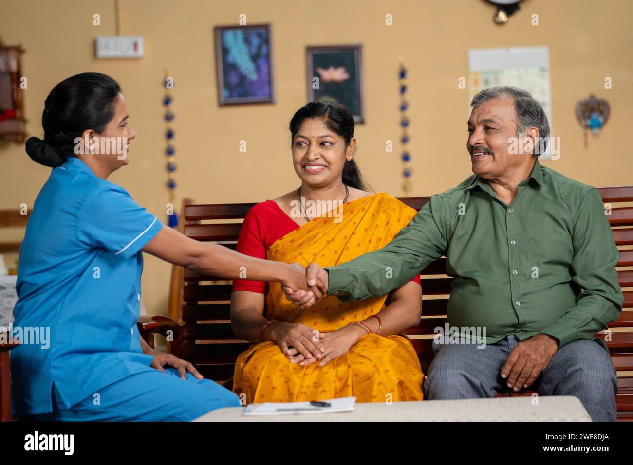 happy Indian nurse or caretaker greeting senior elderly couple at home ...