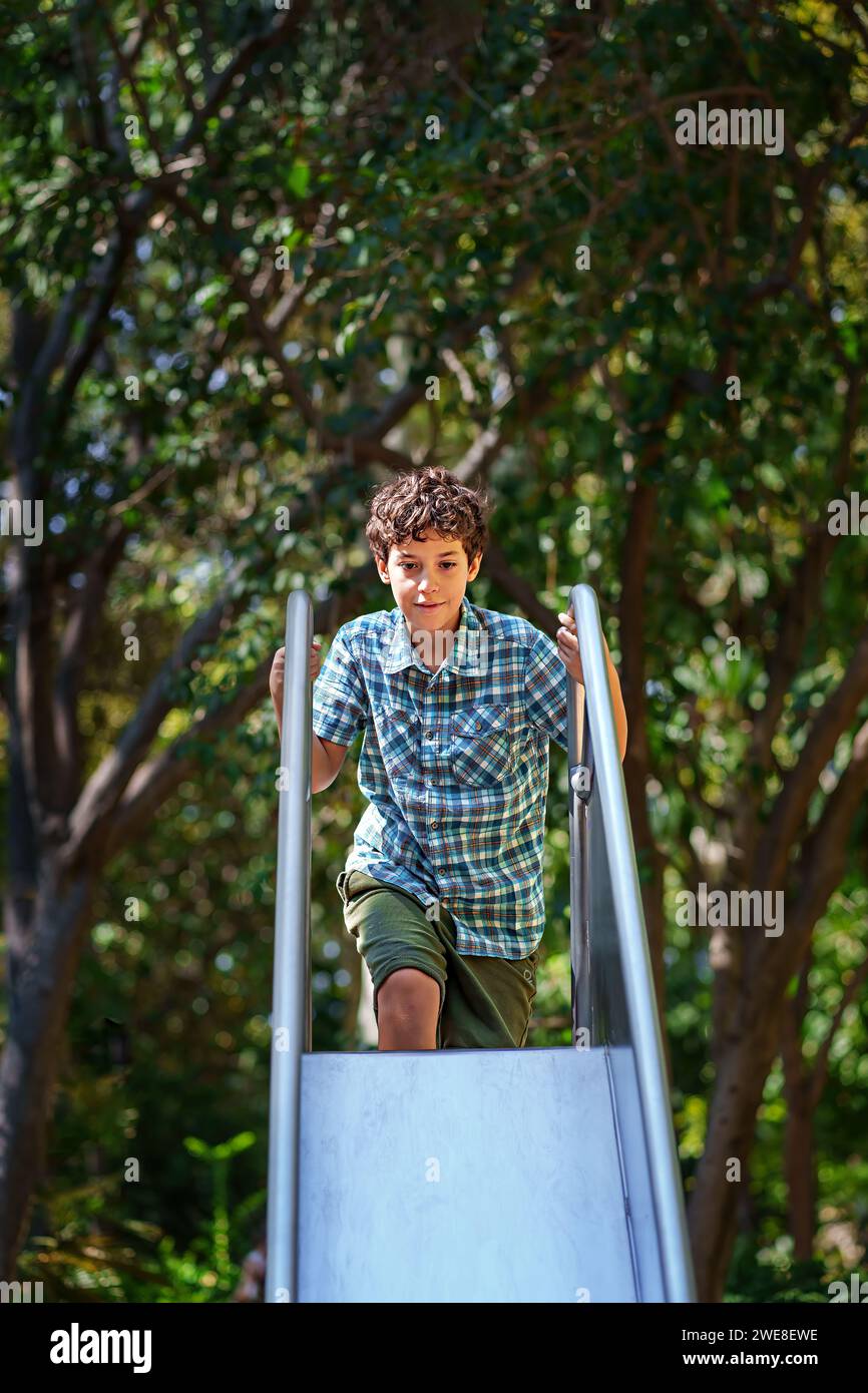 Young boy slides down with joy on a playground slide, surrounded by ...